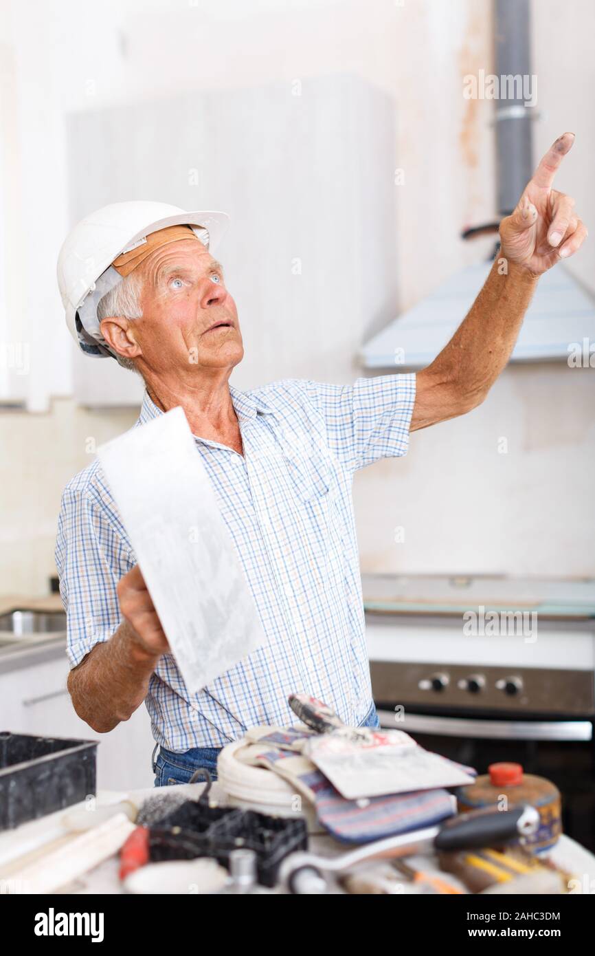 Puzzled aged worker in hardhat working on house overhaul, checking ...