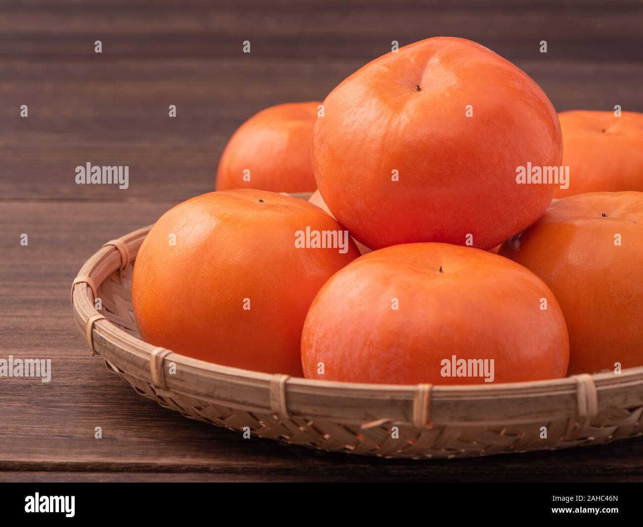 Fresh, beautiful orange color persimmon kaki on bamboo sieve over dark ...