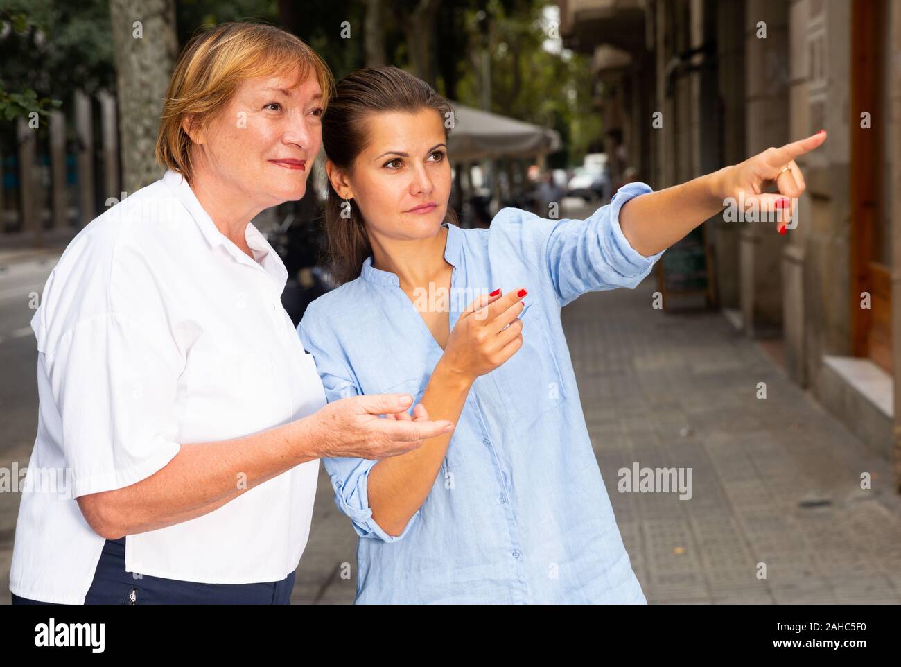 Friendly girl helping mature woman to find necessary address in city ...