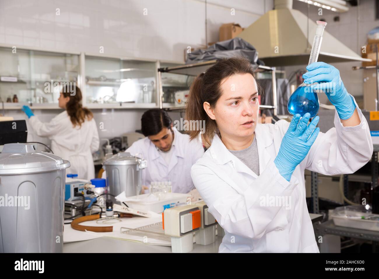 Focused woman lab technician working with reagents in test tubes during ...