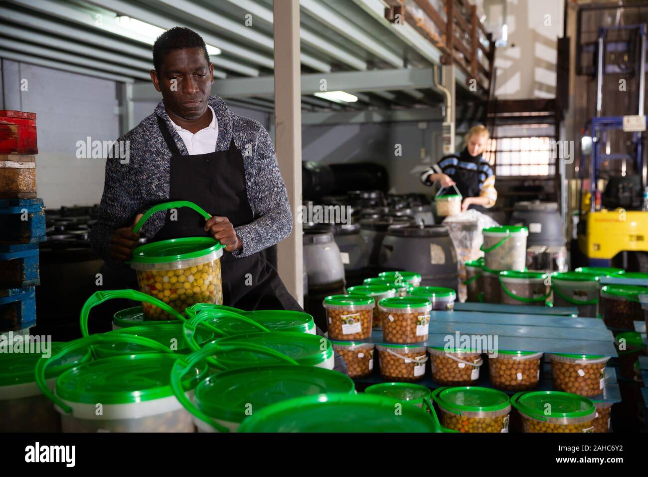 African man worker of pickled olives factory stacking plastic buckets ...