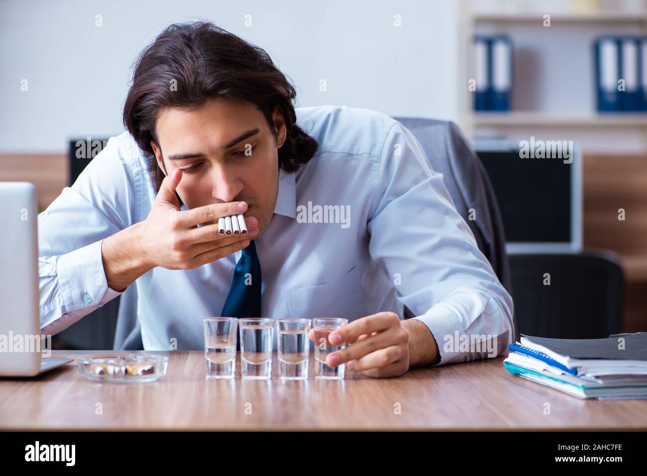 The male employee drinking vodka and smoking cigarettes at workplace ...