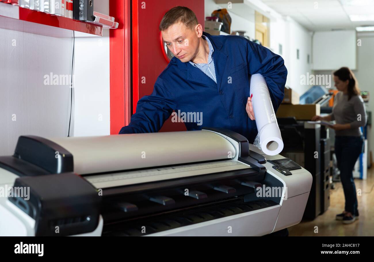 Worker loads new roll of paper into the plotter Stock Photo - Alamy