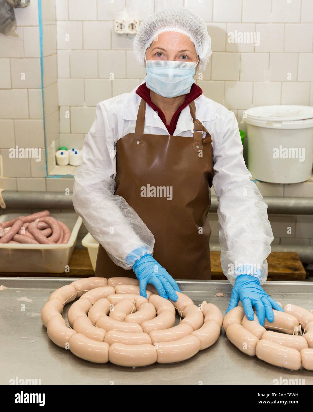 Portrait of workwoman during manual binding of raw sausages before ...