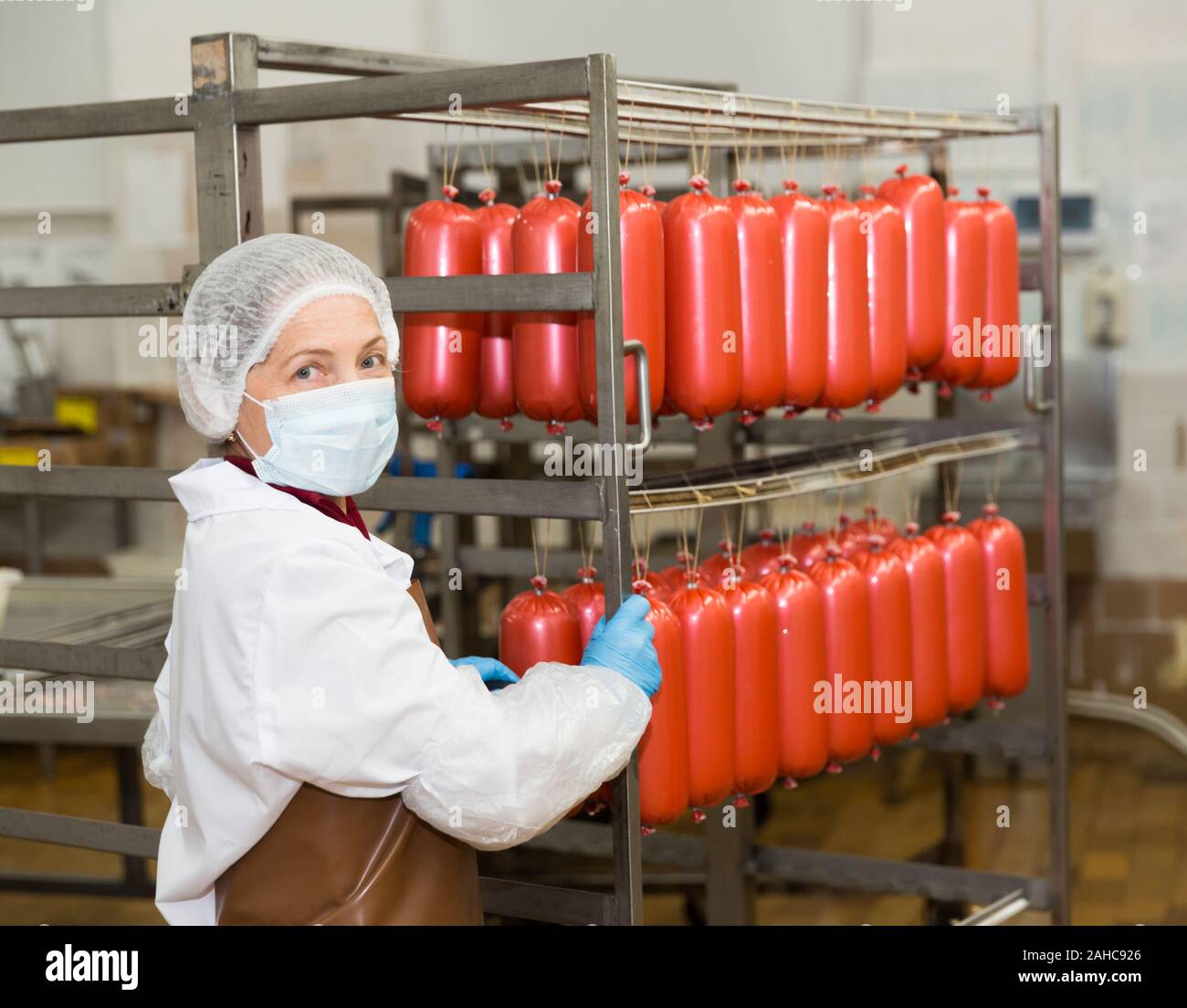 Female worker carrying raw sausages on racks in storage room at meat ...