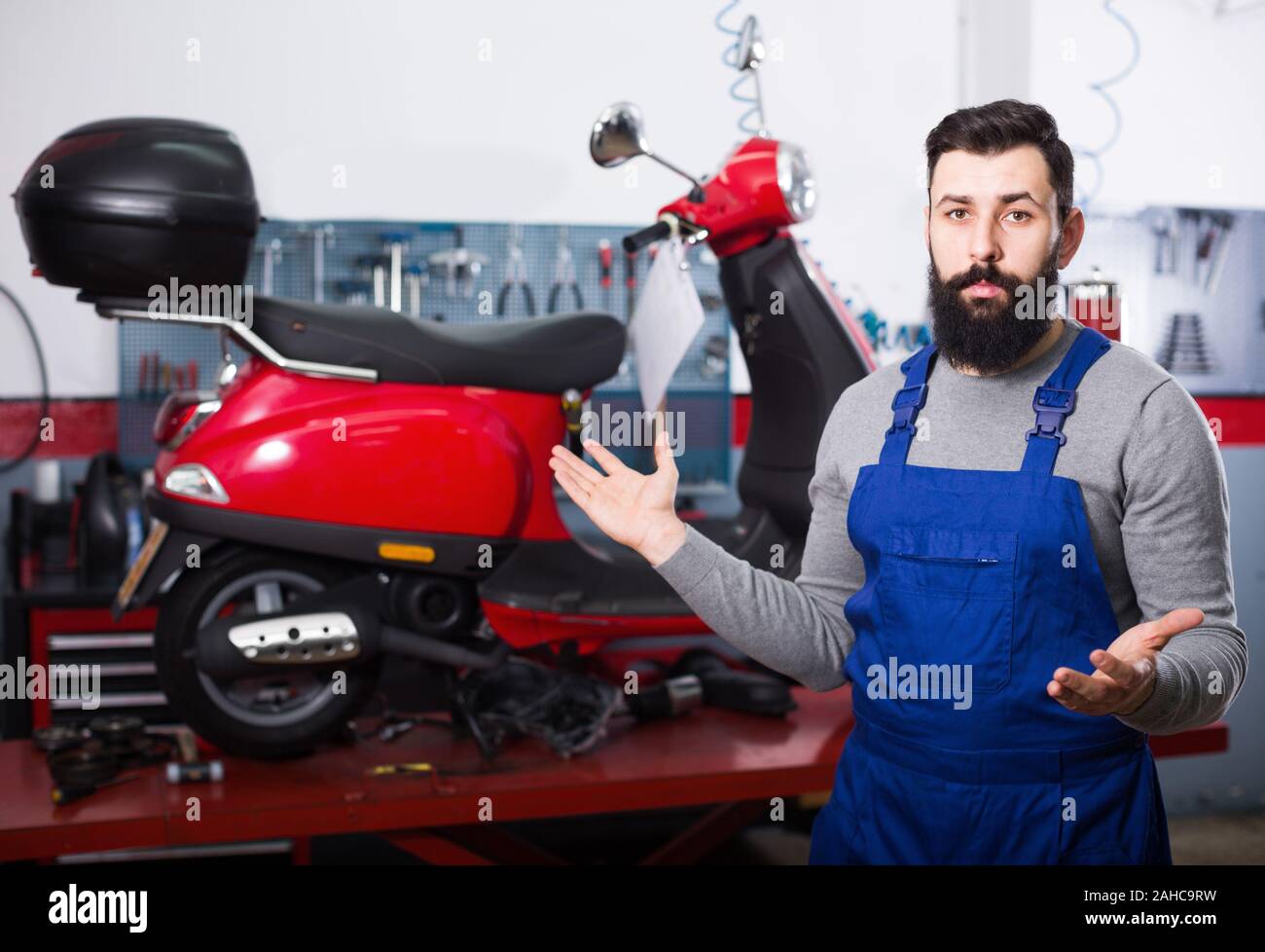 Positive man worker demonstrating motorbikes and scooters in motorcycle ...