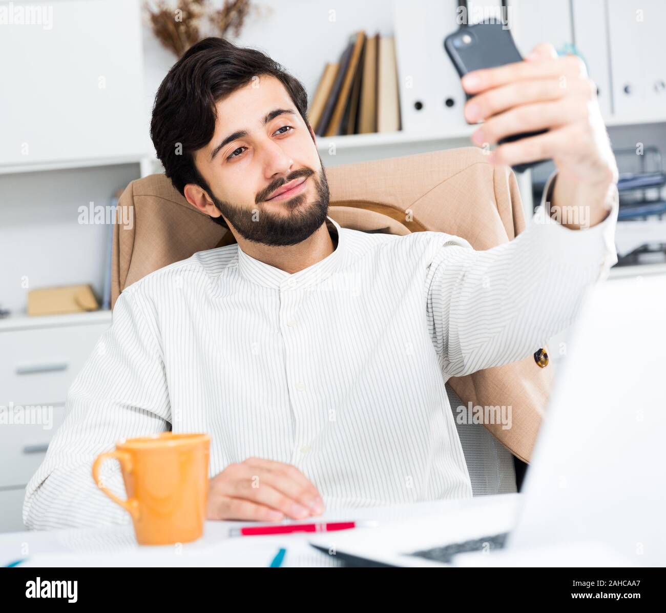 Cheerful young office worker taking selfie on his smartphone at desk in ...