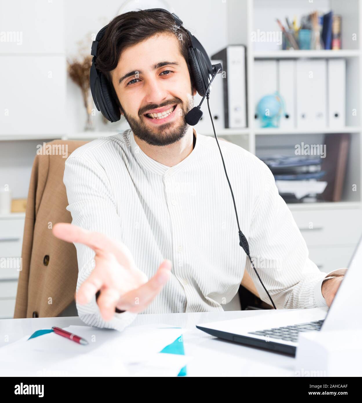 Positive man call center operator with headphones sitting at office ...