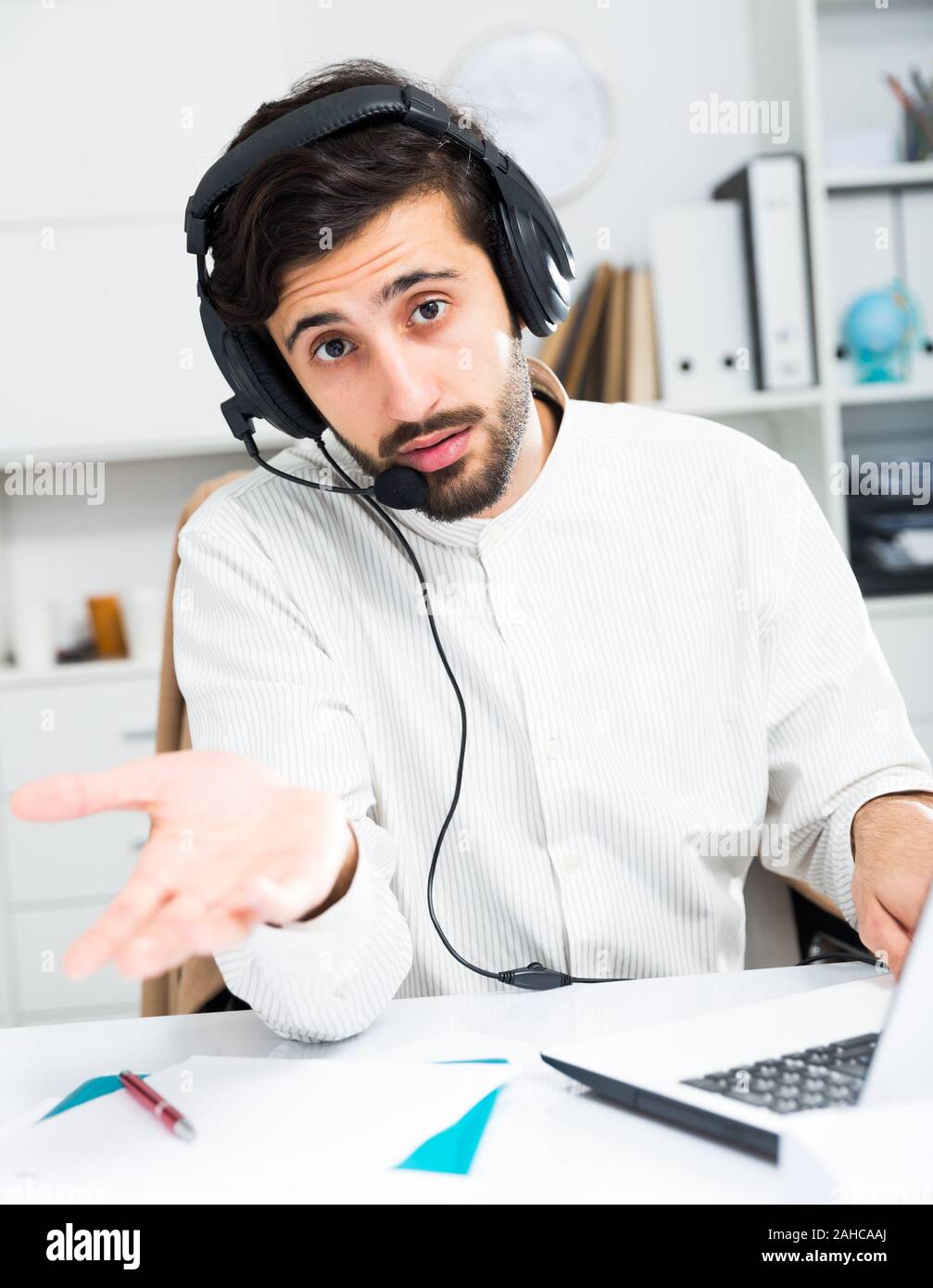 Positive man call center operator with headphones sitting at office ...