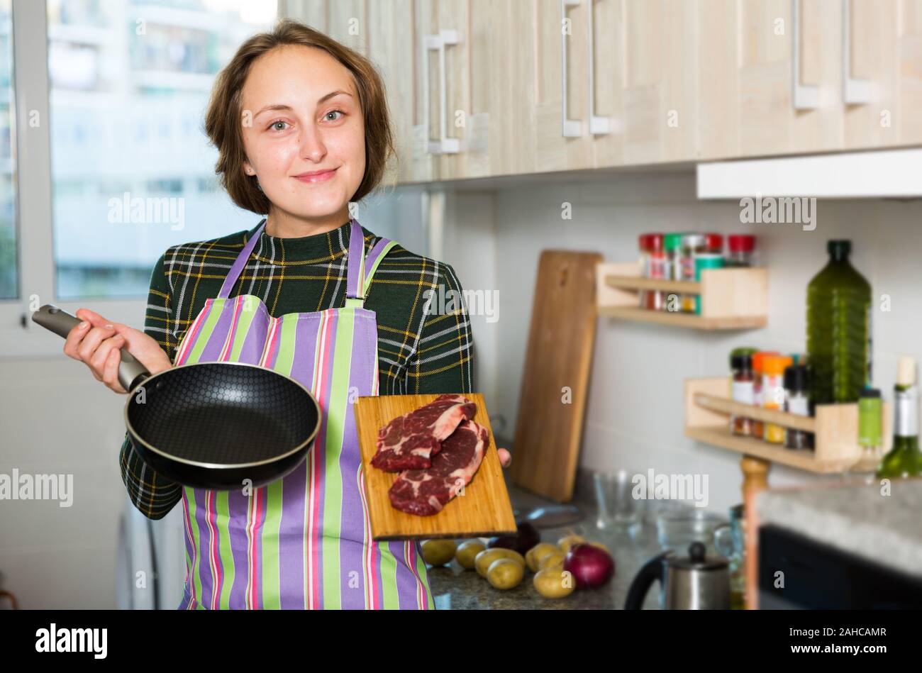 Young lady standing in kitchen while cooking beef chops Stock Photo - Alamy