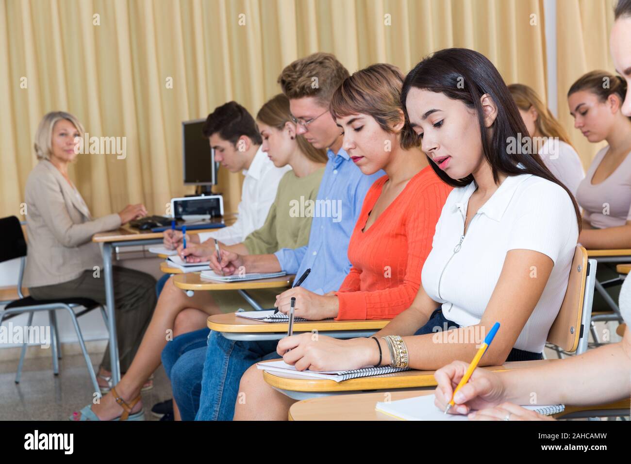 Side view of row of people listening female lecturer and making notes ...