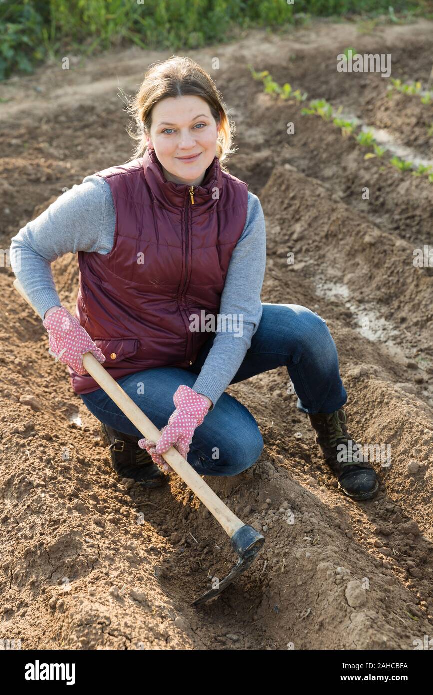 Portrait of adult female worker weeding with hoe beds at organic ...