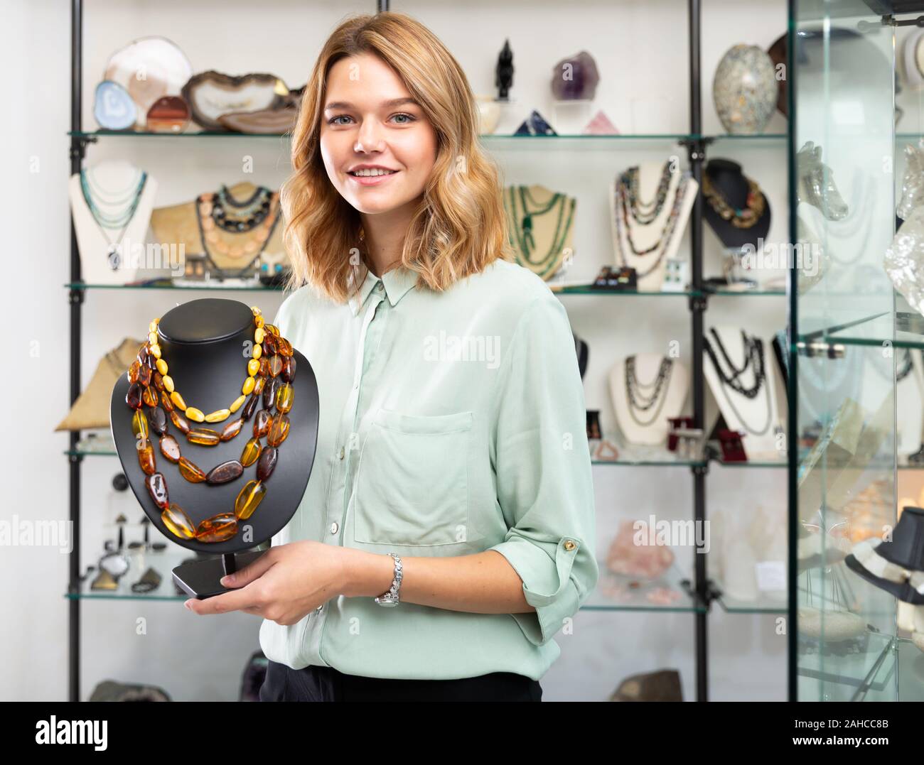 Portrait of cheerful female shop assistant demonstrating amber necklace ...