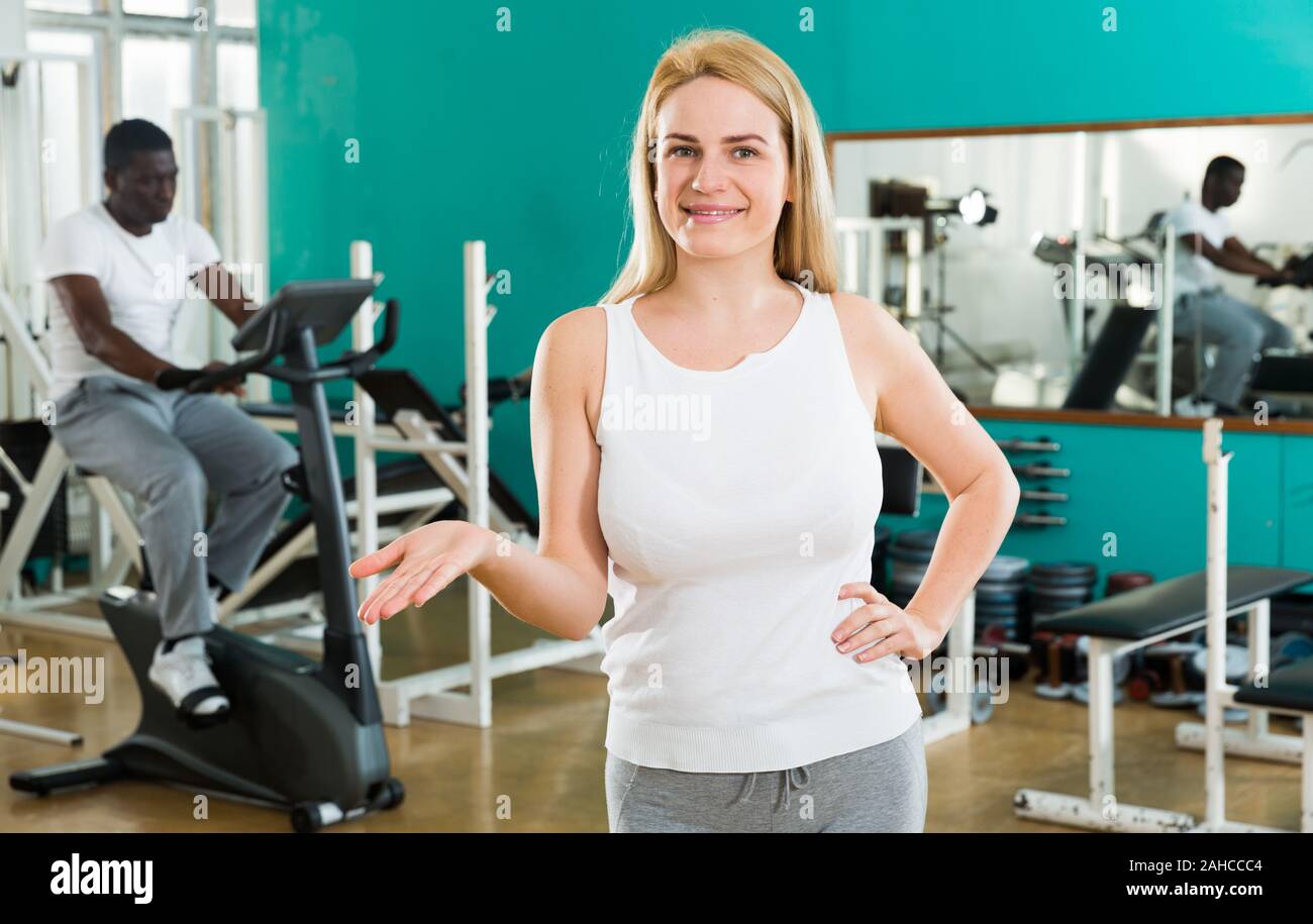 Portrait of positive friendly girl welcoming to gym with exercising man ...