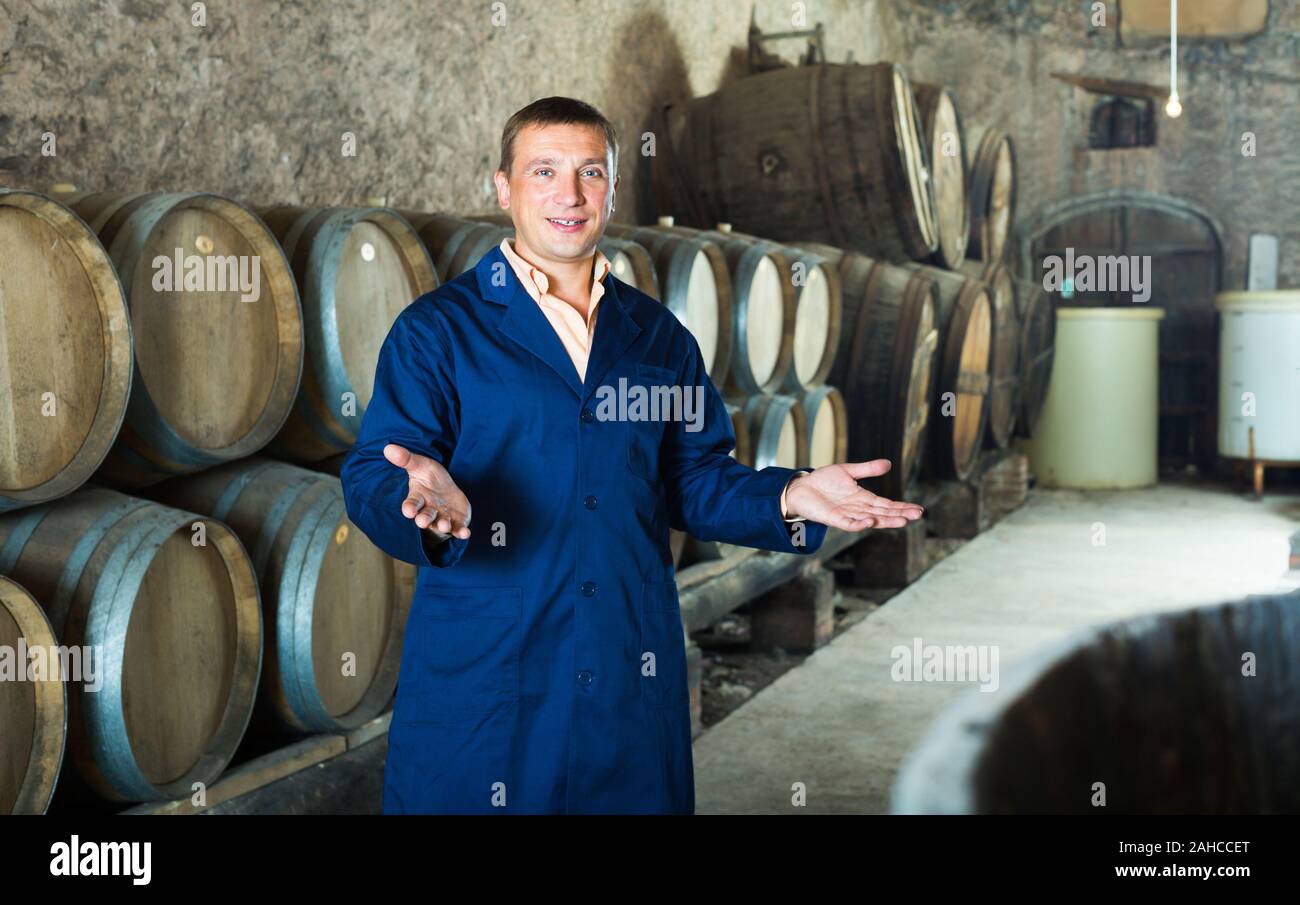 Worker of winery posing with wine barrels in cellar Stock Photo - Alamy