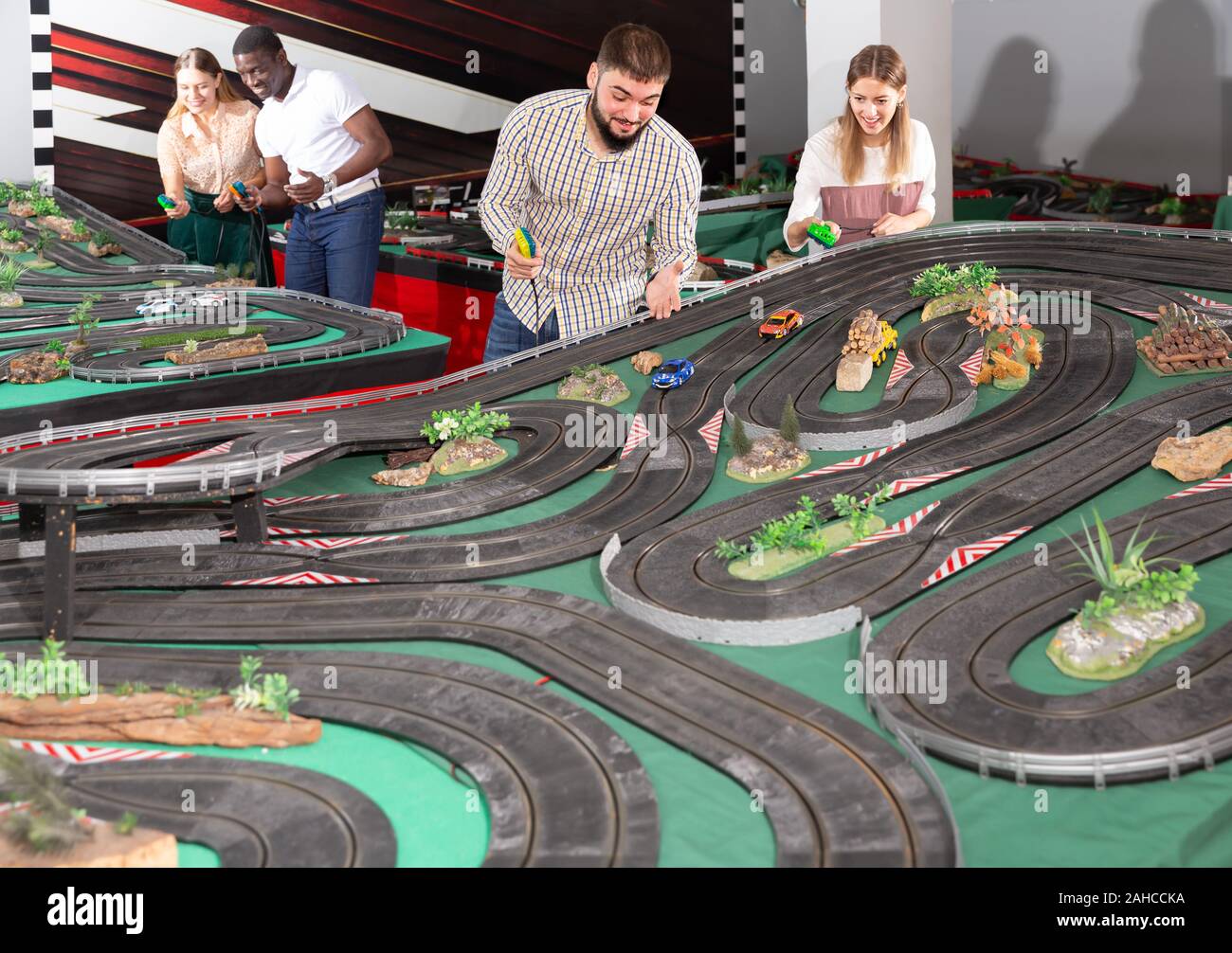 Happy friends enthusiastically remotely control car models on race ...