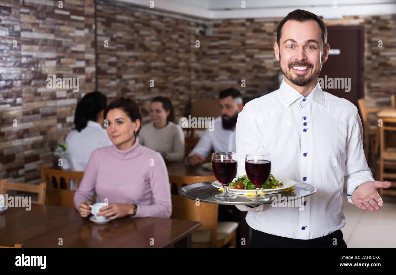 Positive male waiter welcoming guests to rustic restaurant Stock Photo ...