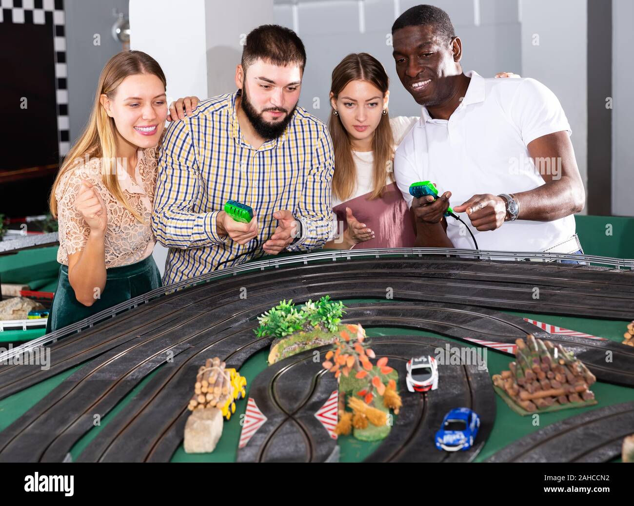 Team of adult boys and girls is playing with slot car model racing ...