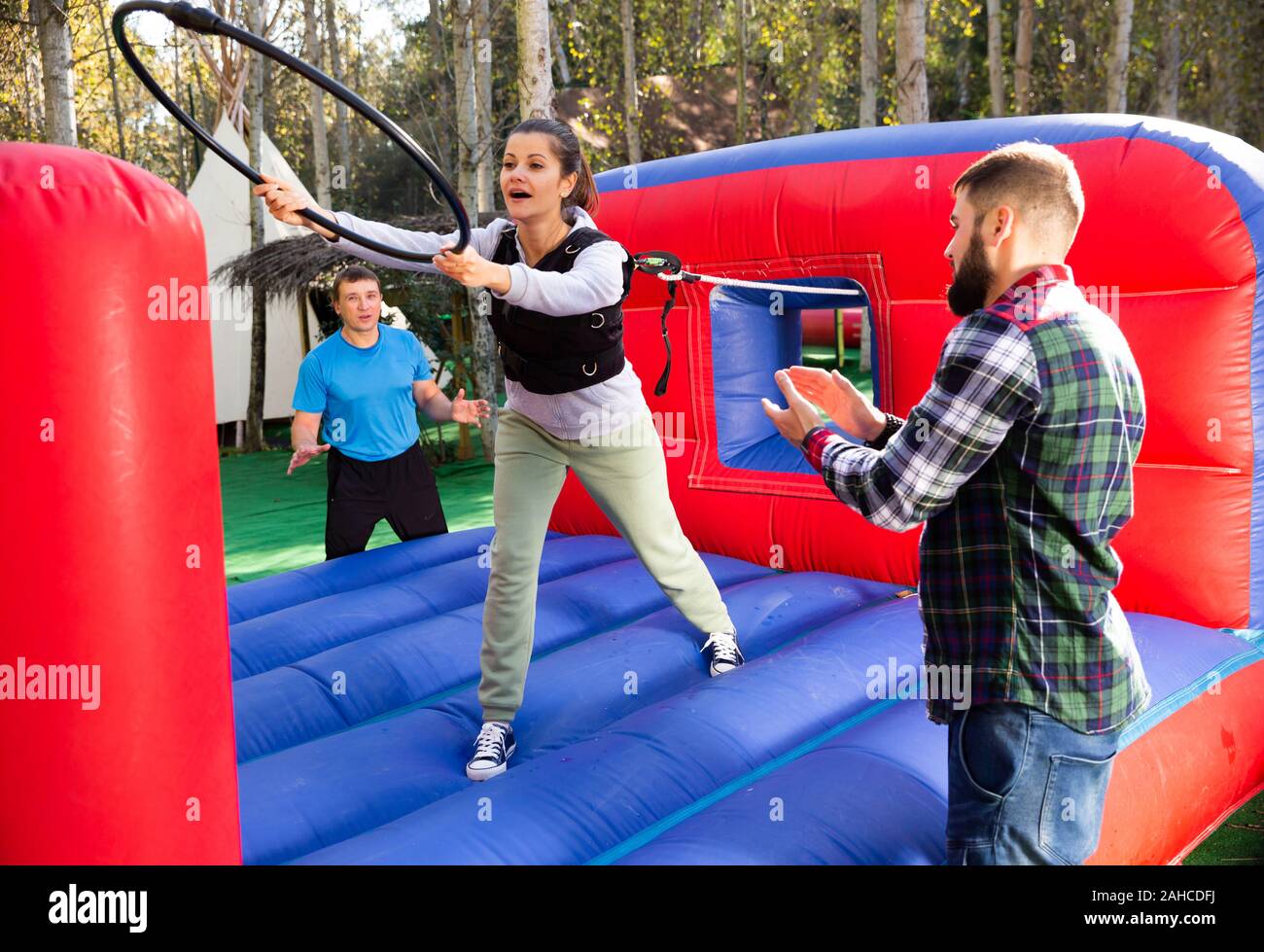 Cheerful woman playing tug of war with hoop on inflatable arena in ...