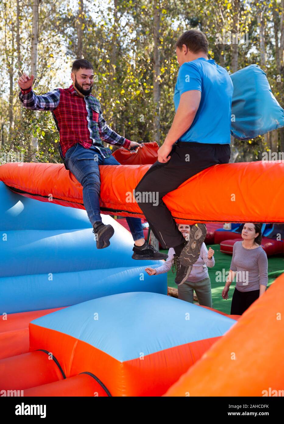 Guys having funny wrestling by pillows on inflatable beam in outdoor ...