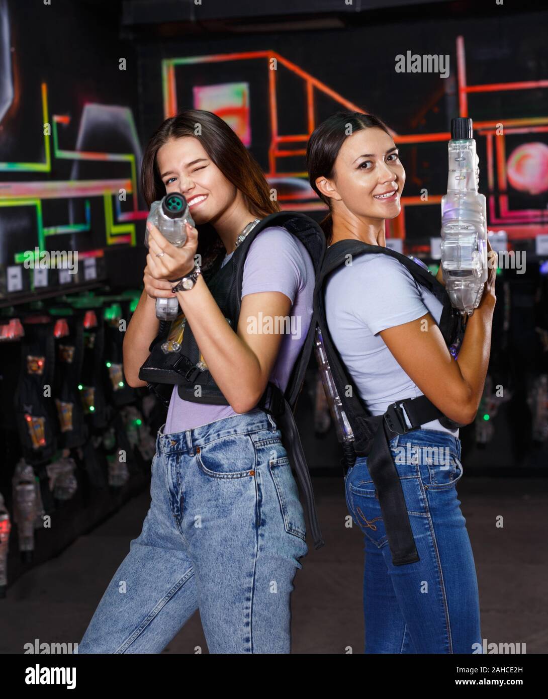 Two positive glad smiling girls standing back and holding guns during ...