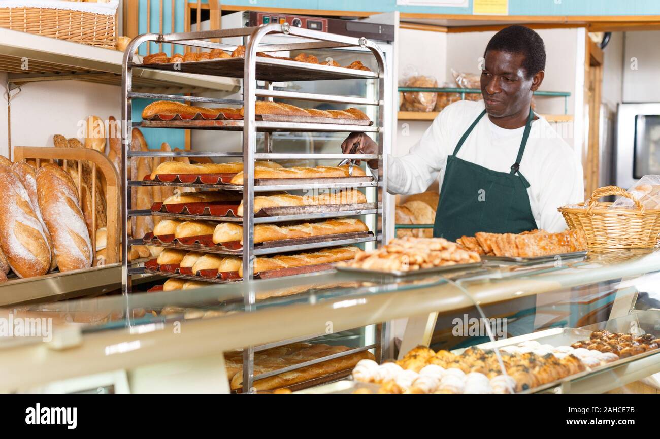 Skillful African American baker working in small bakery, arranging ...