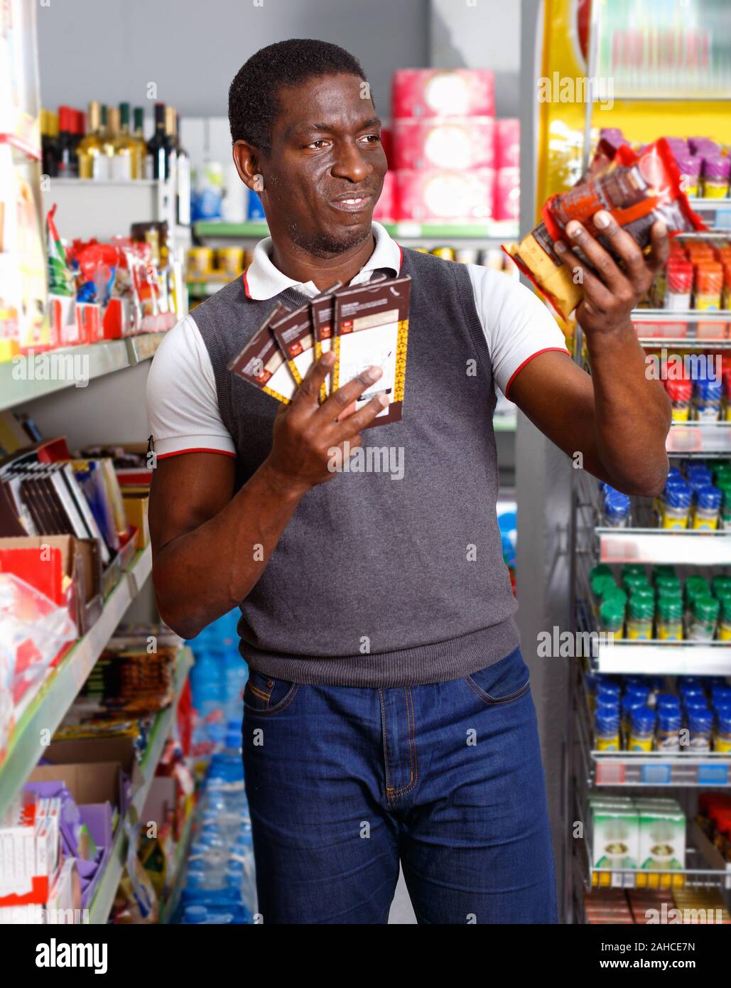 Portrait of cheerful positive Afro man buying chocolate sweets in store ...