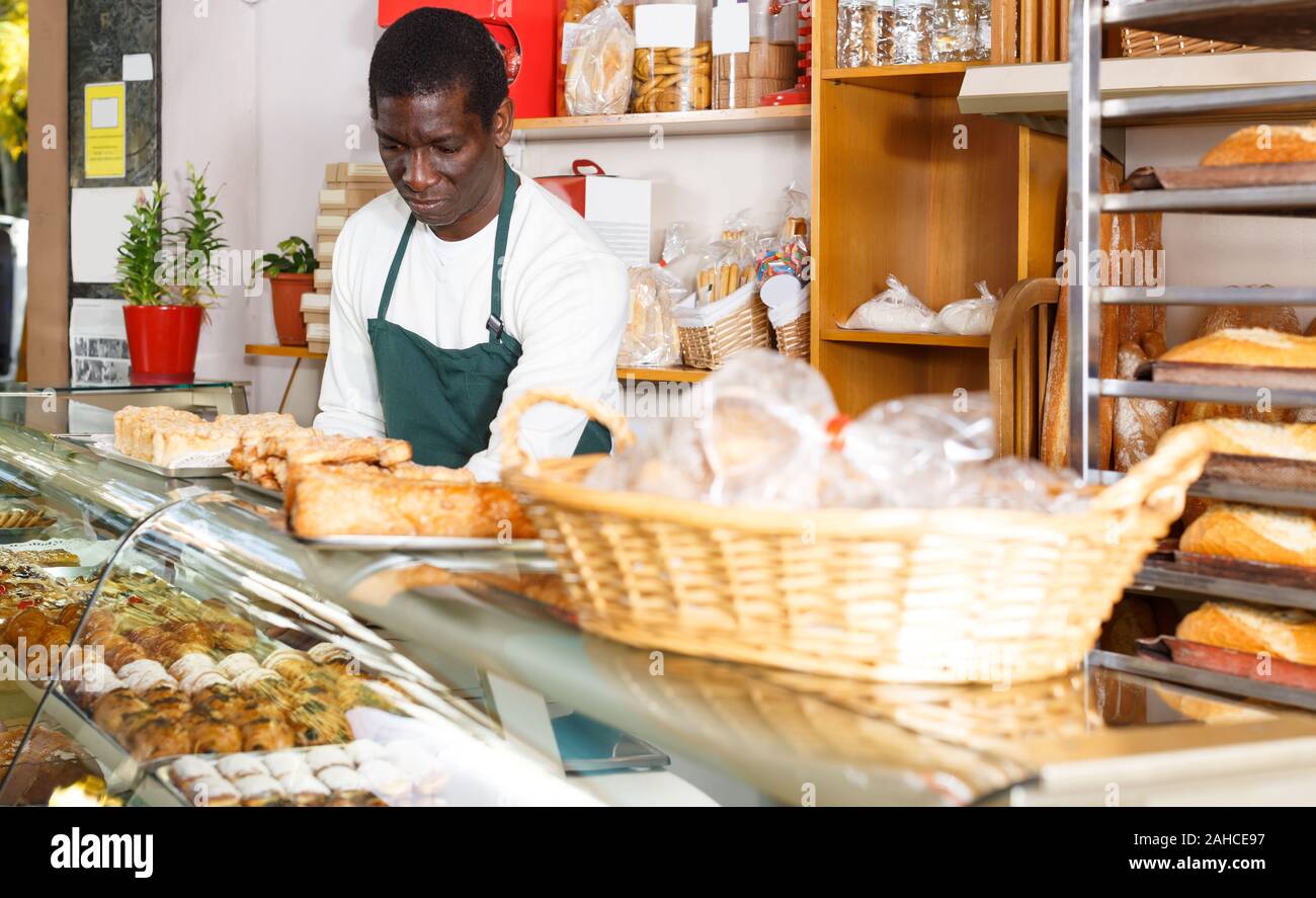 Adult African American baker working in small bakery, arranging ...