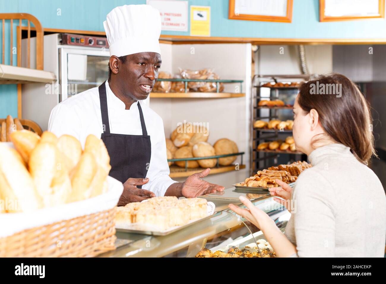 Professional baker standing at counter in bakehouse, selling baked ...