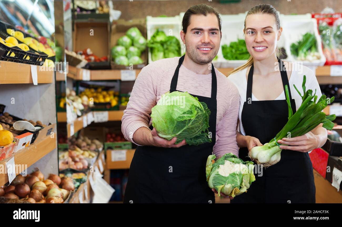 Young smiling man and woman sellers showing green onion and cabbage in ...