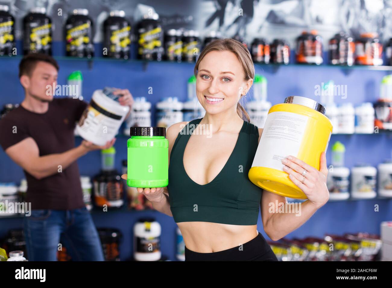 Cheerful bodybuilder girl holding plastic jar of sport food supplements ...