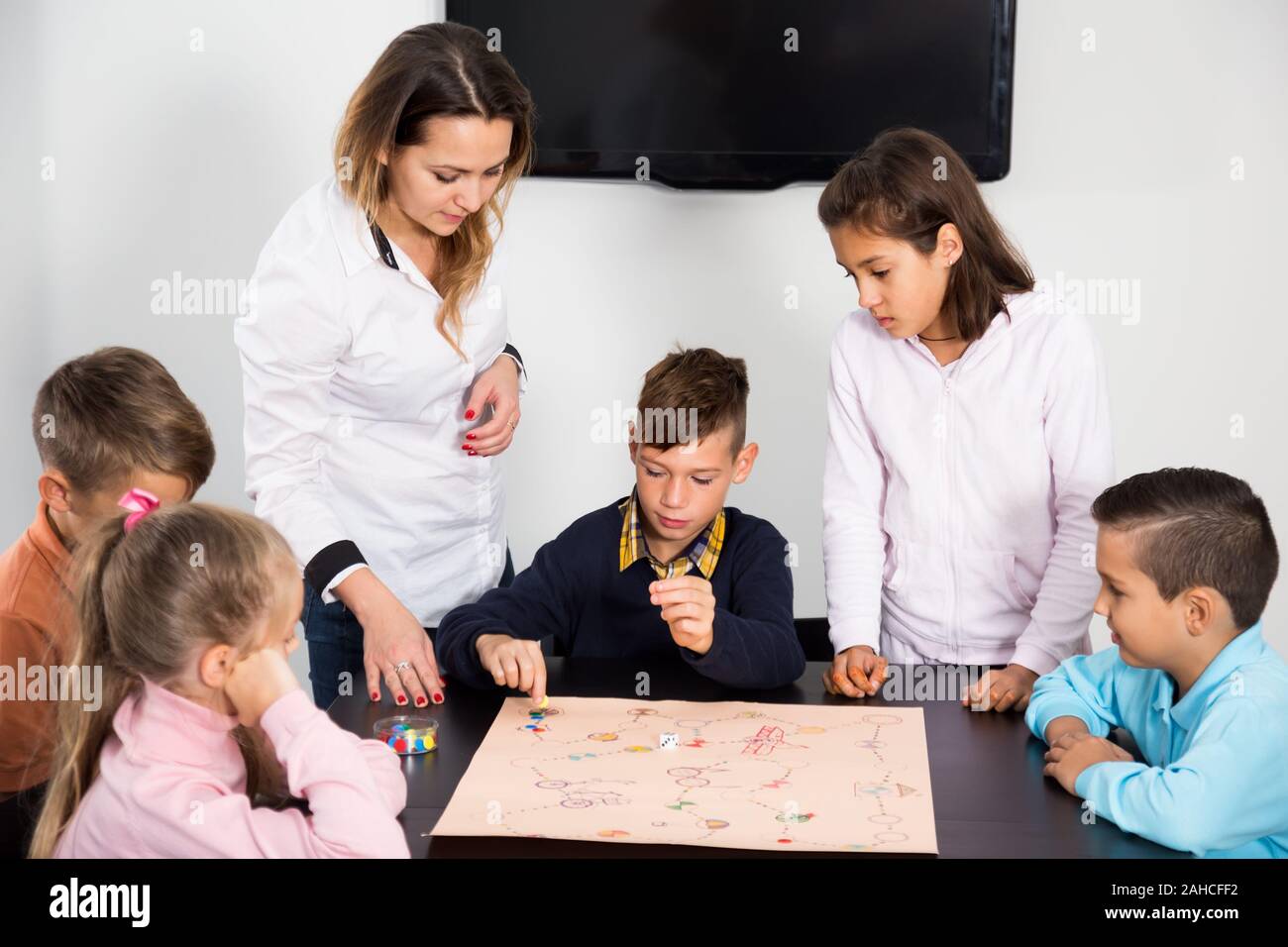 Happy kids sitting at table with board game and dice at school class ...