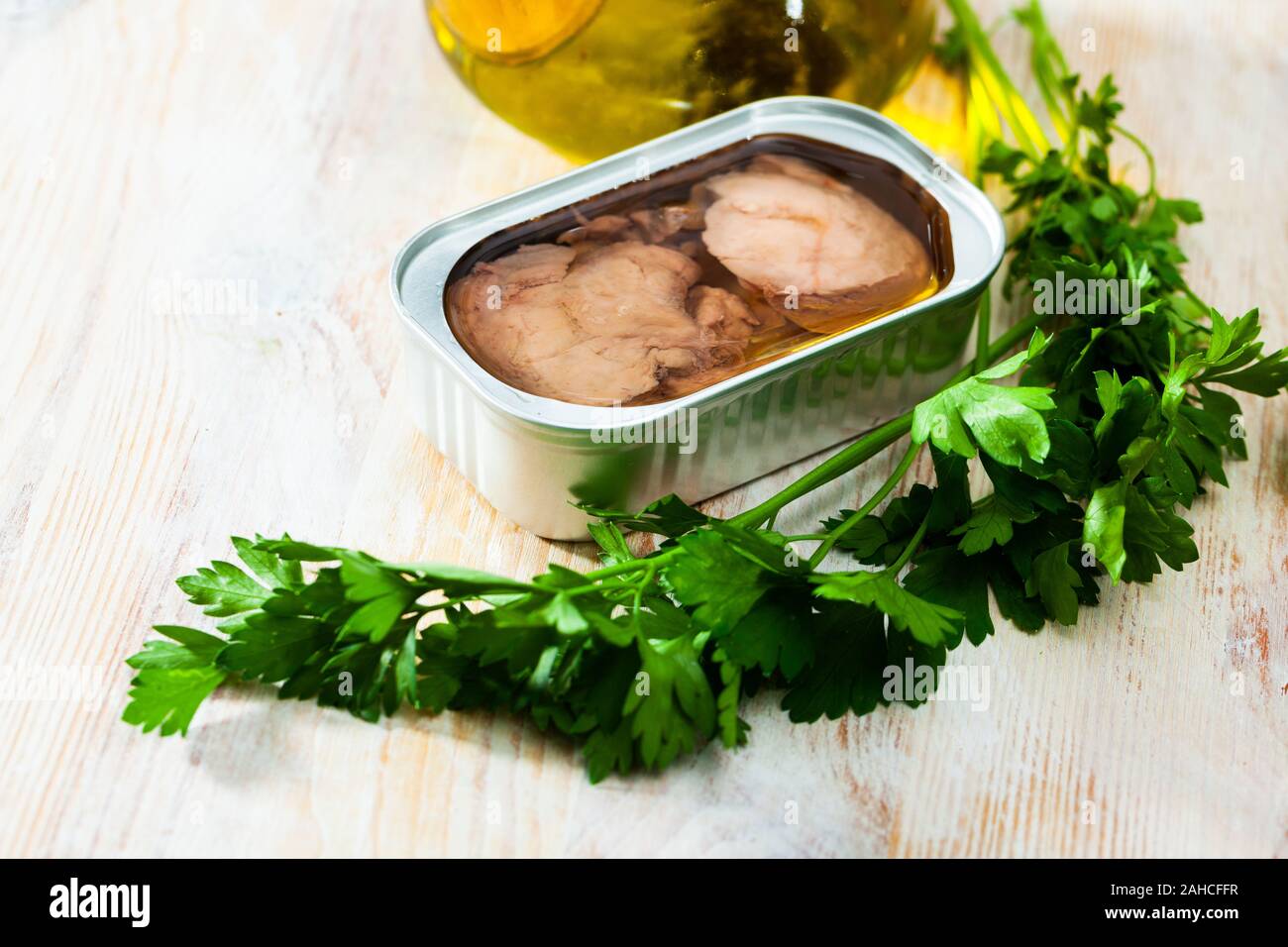 Smoked cod liver in oil in open tin can with fresh greens on wooden ...