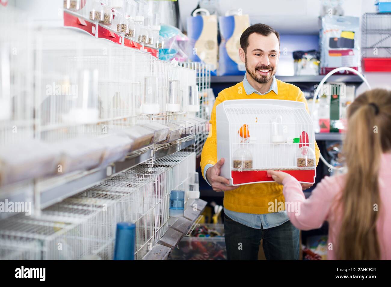 happy man seller demonstrating canary bird in cage to girl in pet shop ...