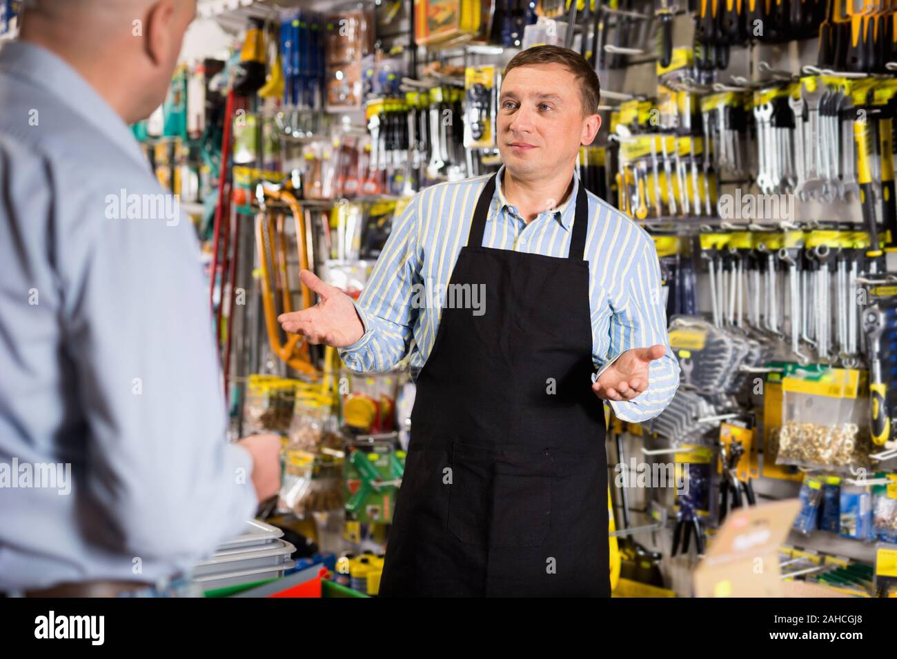 Adult glad smiling salesman offering tools to man Stock Photo - Alamy