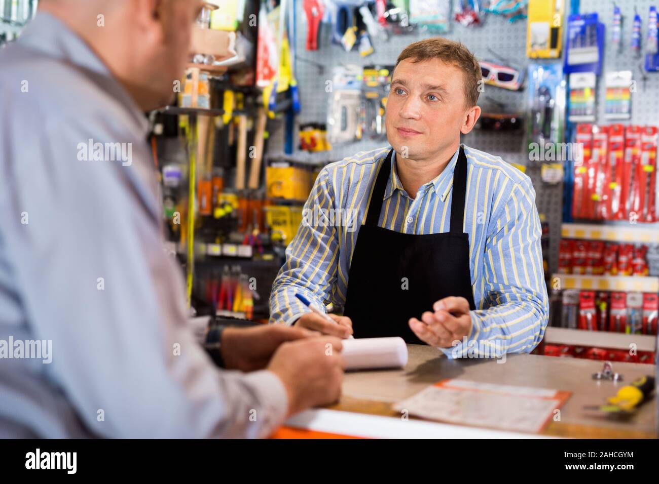 Adult glad salesman offering tools to man Stock Photo - Alamy
