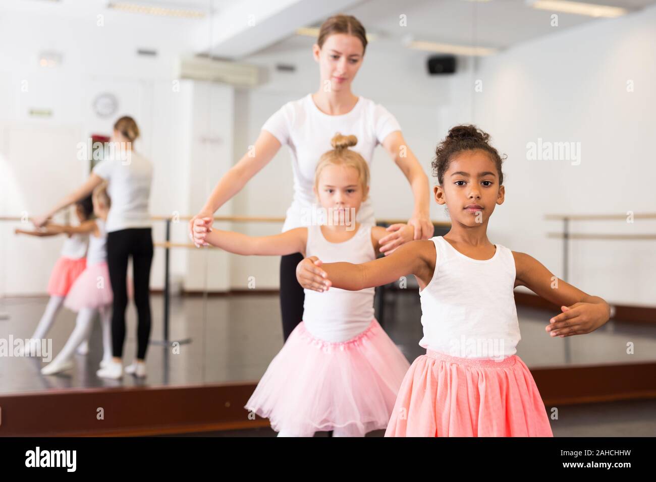 Young female classical dance teacher helping her little girls students ...