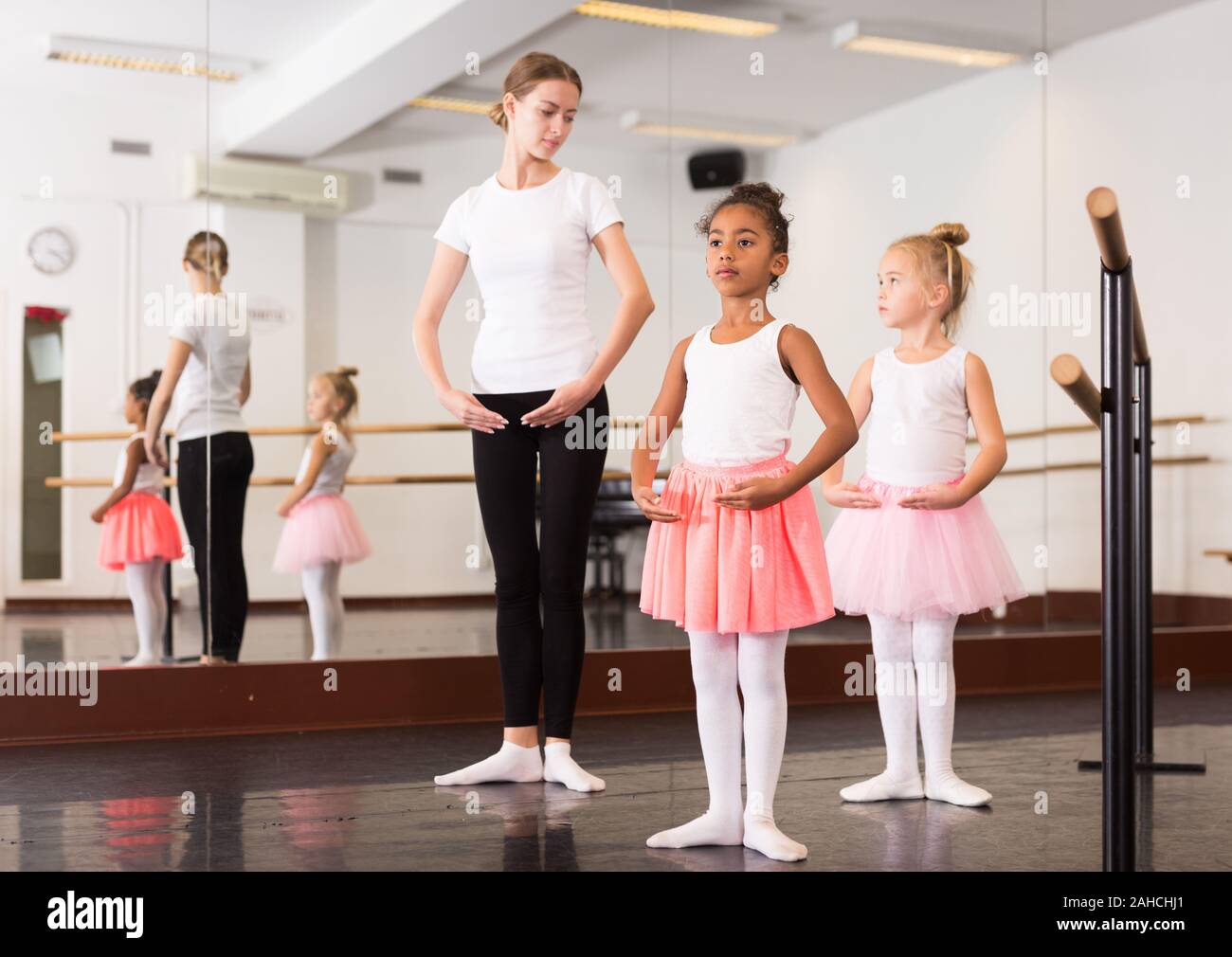 Young female classical dance teacher helping her little girls students ...