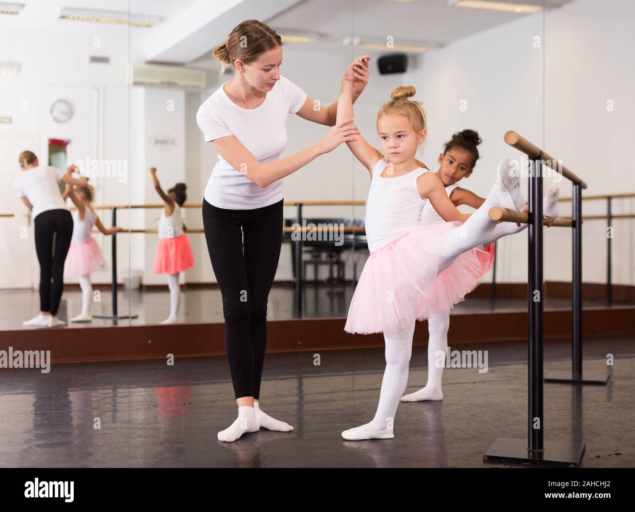 Female ballet trainer teaching two little girls near ballet barre in ...