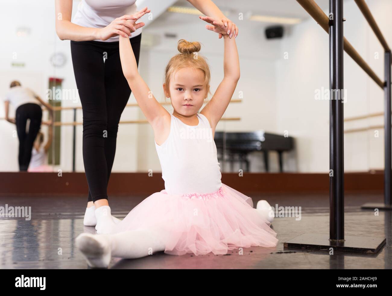 Little ballerina practicing front splits position with help of young ...