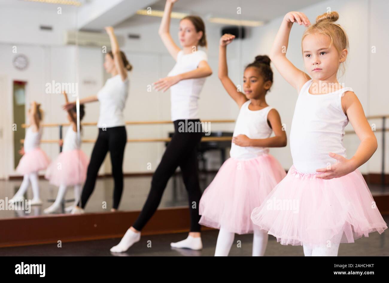 Young female classical dance teacher helping her little girls students ...