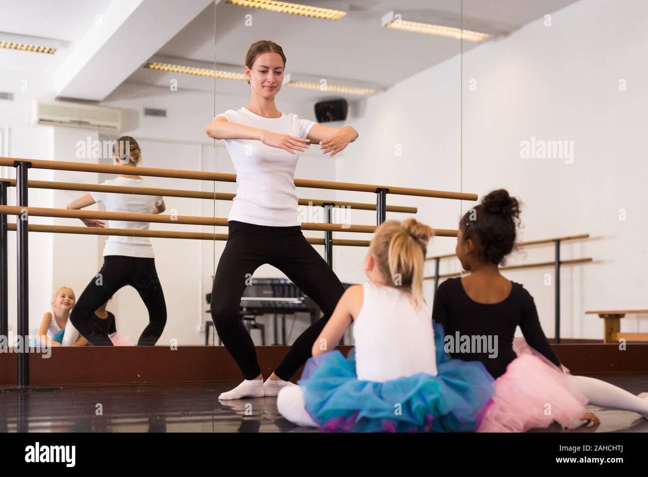 Female ballet teacher demonstrating choreographic element to two little ...