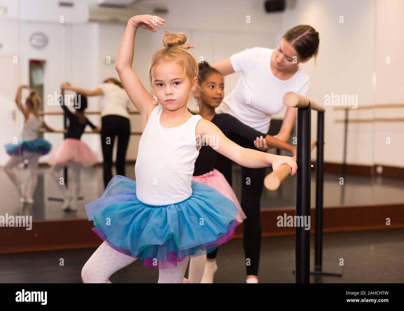 Young female classical dance teacher helping her little students near ...