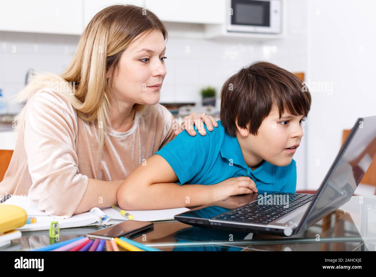 Woman helping tweenage boy with lessons sitting together at home ...