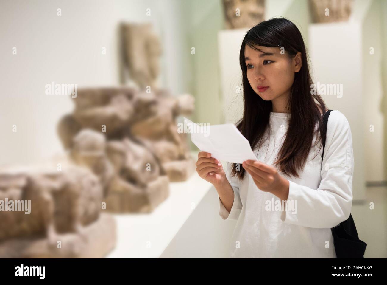 Young chinese woman visitor with guide book looking at exhibition in ...