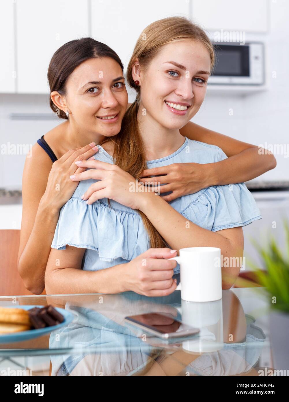 Young smiling emotional girlfriends hugging and having fun at table at ...