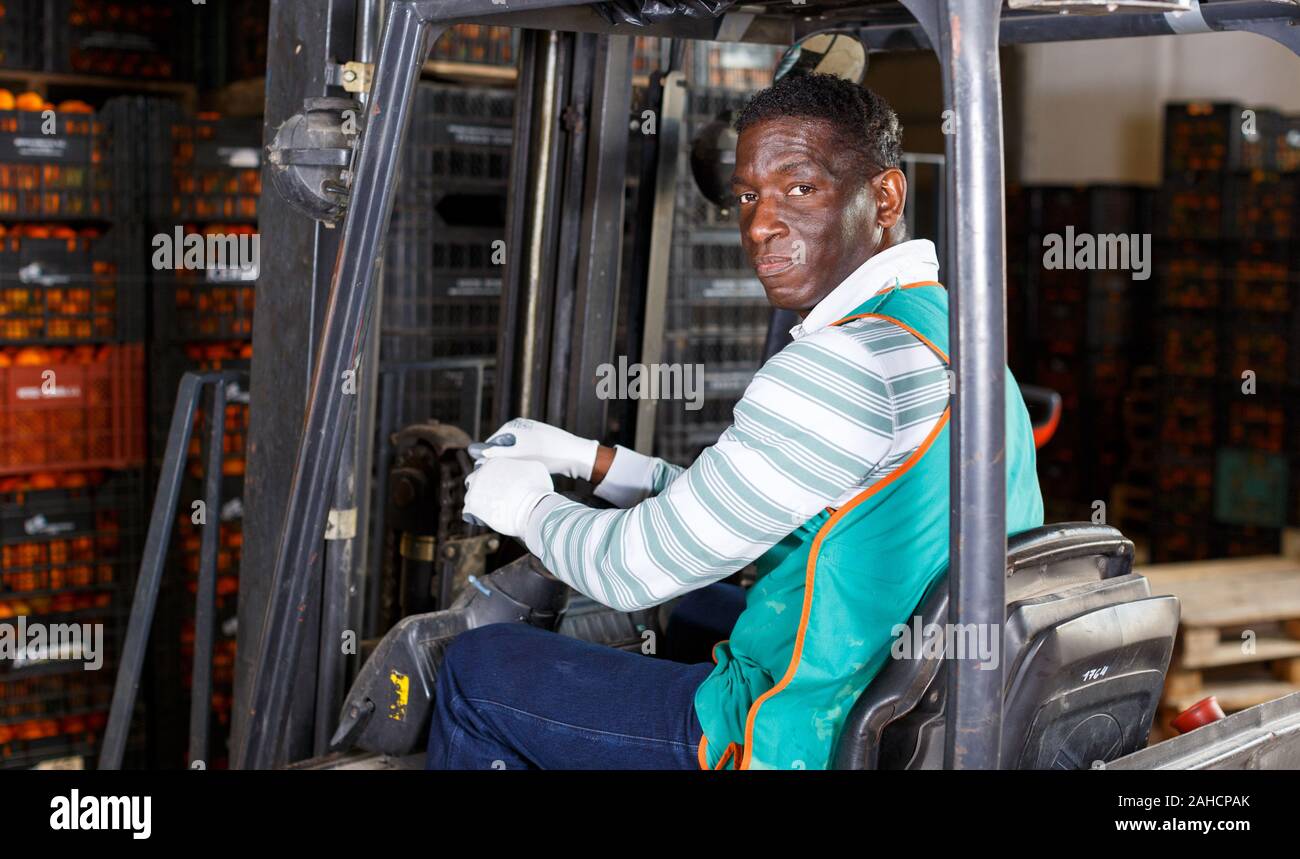 Portrait of afro man posing near stacker in warehouse with mandarins ...