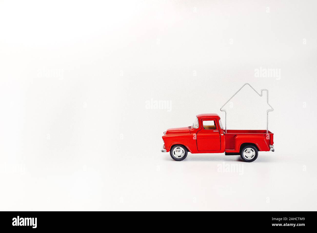 miniature red retro car pickup driven by a house isolated on a white ...