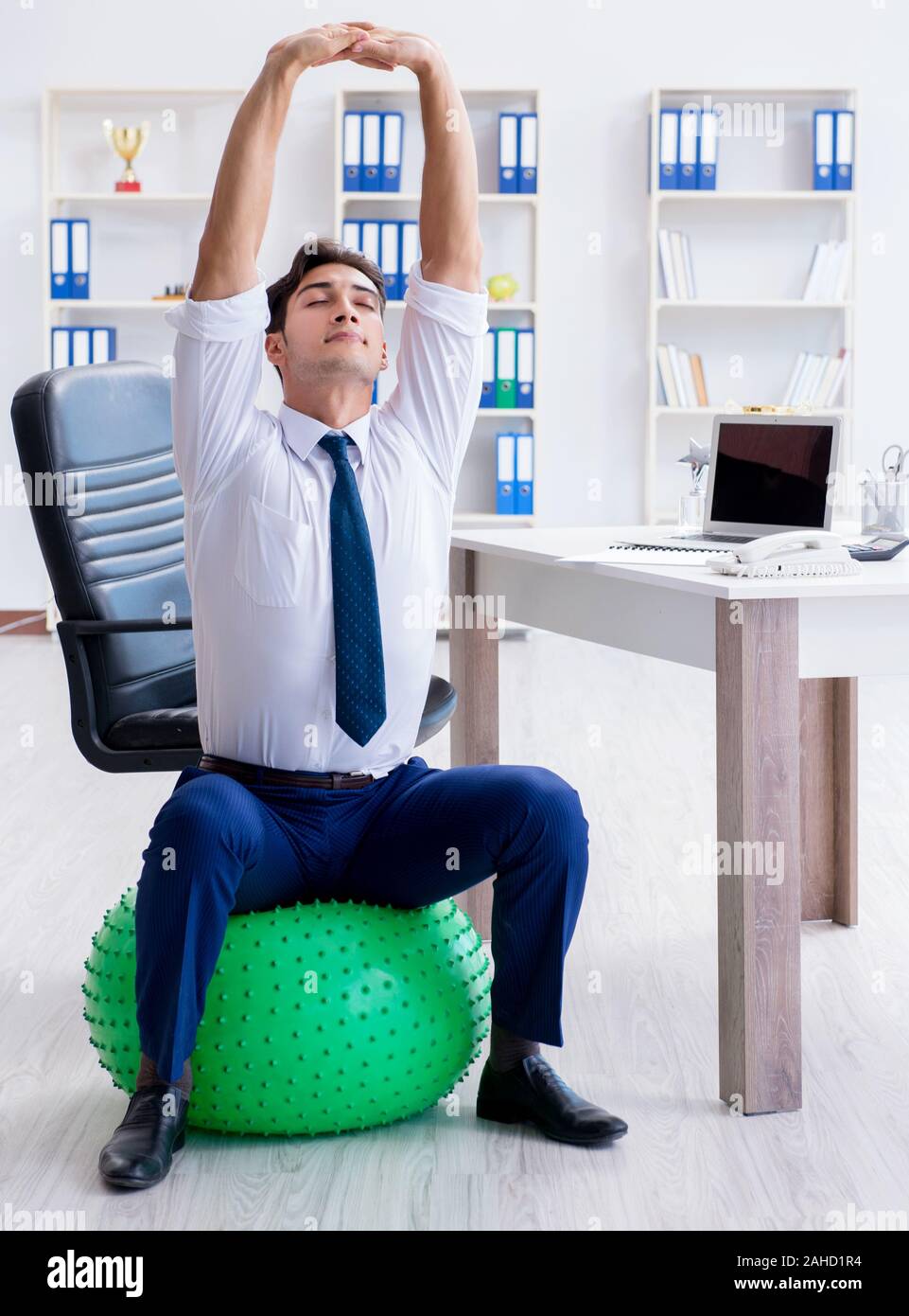 The young businessman doing sports stretching at workplace Stock Photo ...