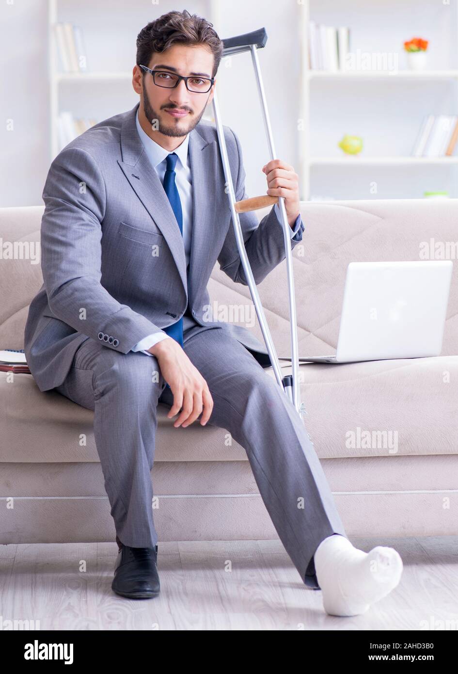 The businessman with crutches and broken leg at home working Stock ...